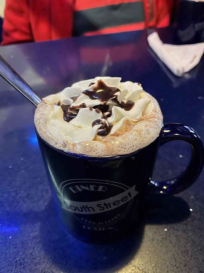 Hot chocolate topped with whipped cream and chocolate drizzle in a branded mug is pure liquid comfort.