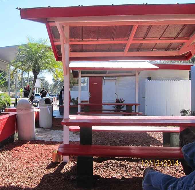 Red picnic tables under shade provide the perfect stage for your epic sandwich consumption performance today.