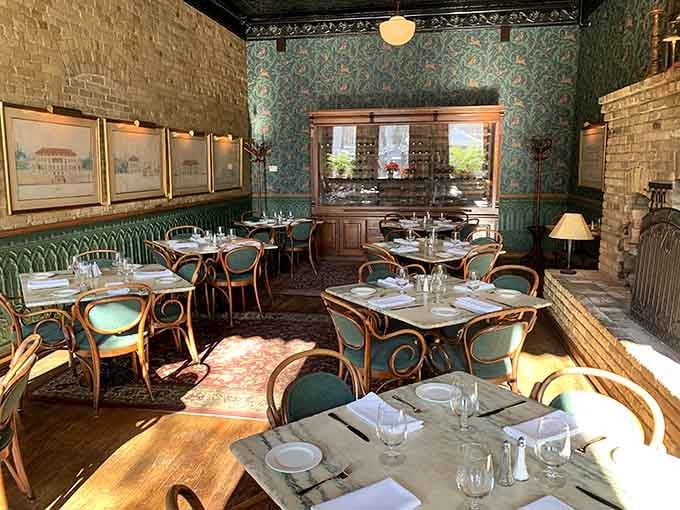 Teal upholstered banquettes and bentwood chairs under ornate wallpaper make every meal feel like a special occasion worth remembering.