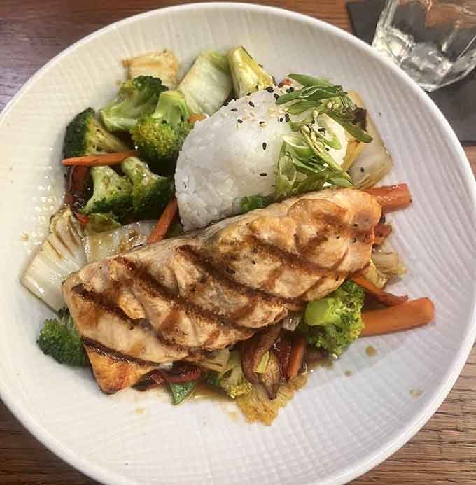 Grilled salmon over stir-fried vegetables with rice creates a balanced plate that looks as good as it tastes.