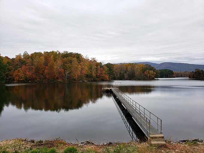 The metal fishing pier extends like a welcoming handshake into autumn-kissed waters where bass and bluegill await below.