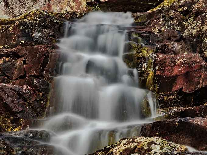 Close-up, the waterfall reveals intricate patterns as water finds its path through ancient stone with timeless grace.