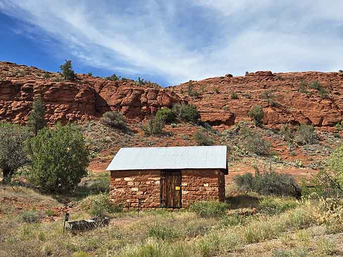 A stone cabin sits quietly against layered red cliffs, looking like it's been waiting for Clint Eastwood to ride past.