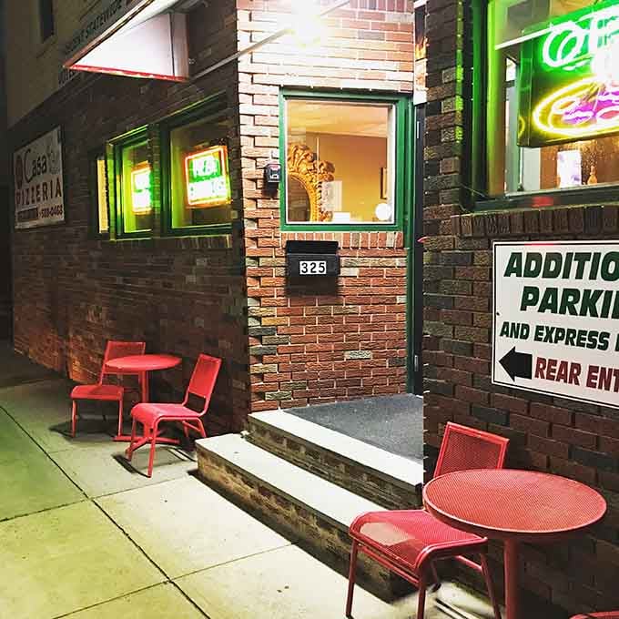 Red outdoor tables on the sidewalk offer the perfect spot for enjoying your pizza on a pleasant evening.
