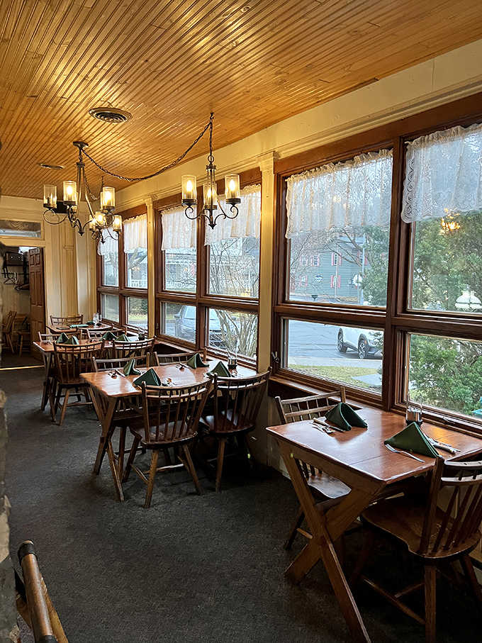 Sunlight streams through tall windows onto wooden tables set with green napkins, creating an inviting spot for any meal.