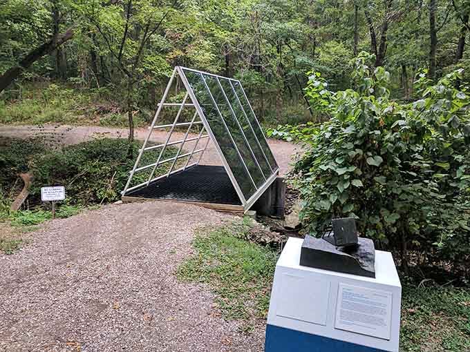 A triangular bridge sculpture nestled in the woods, leading nowhere but looking absolutely perfect doing it anyway.