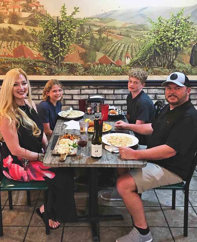 Four happy diners beneath a Tuscan mural, proving that good Italian food brings families together since time immemorial.