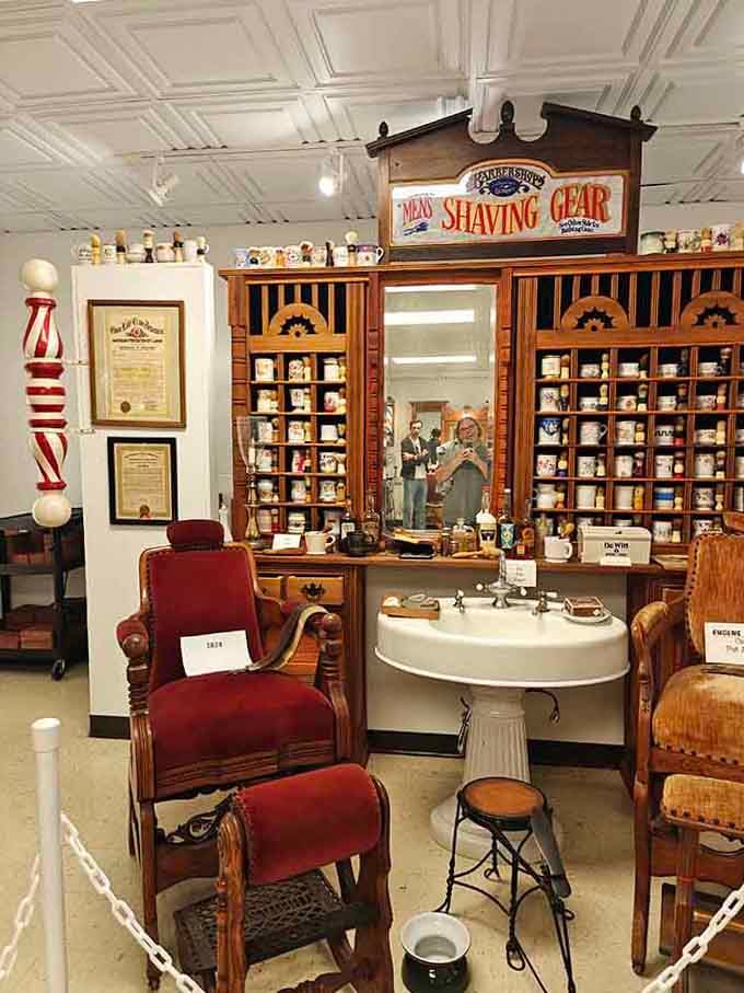 An ornate shaving gear cabinet towers over vintage chairs, showcasing the impressive array of products barbers once offered their customers.