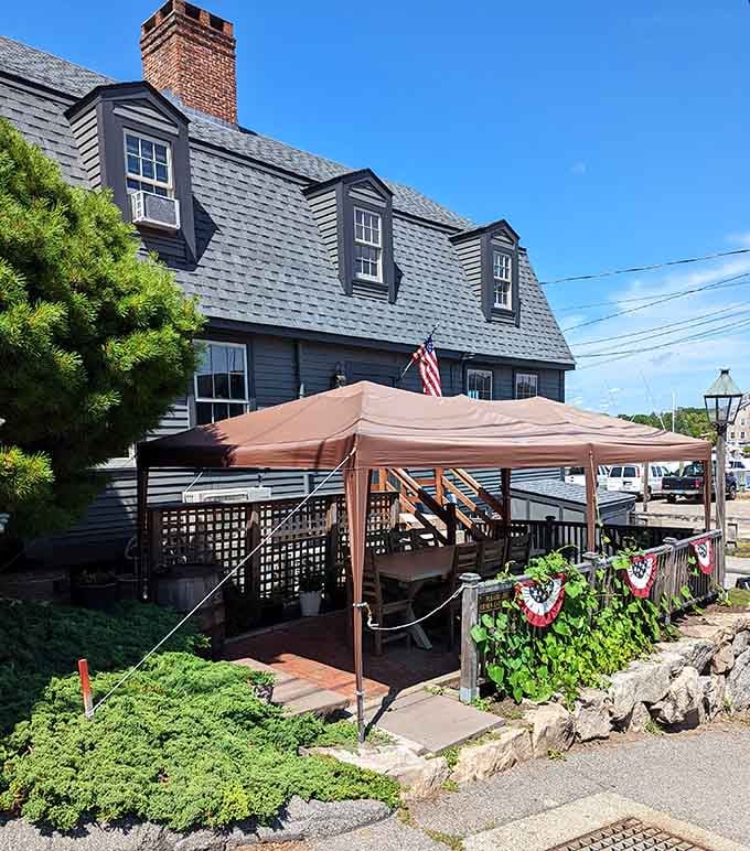 The waterside patio with cheerful umbrellas offers alfresco dining where colonial charm meets modern comfort under sunny Connecticut skies.