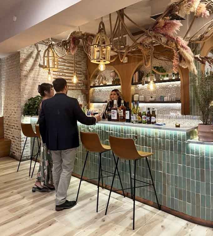 The bar area glows with mint-green tiles and rustic branches overhead, mixing garden party with sophisticated cocktail lounge vibes.