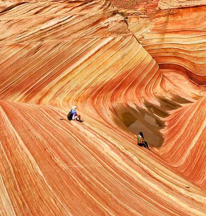 Two visitors sit dwarfed by swirling stone, contemplating how wind and water created this masterpiece slowly.