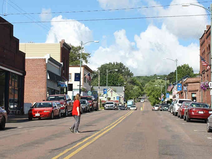 Main Street stretches toward rolling hills where brick storefronts stand proud under billowing clouds and endless blue sky.