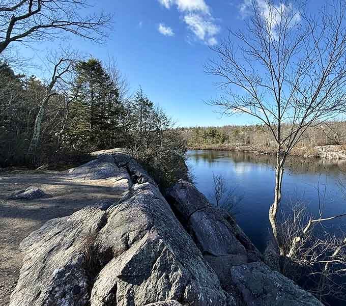 Ancient glacial rocks frame this mirror-smooth water under brilliant blue skies, rewarding those who made the climb.