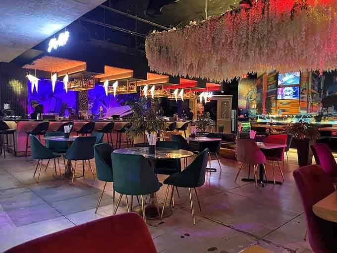 Pink and teal velvet chairs under cascading blossoms create an atmosphere that's equal parts sophisticated lounge and whimsical wonderland.