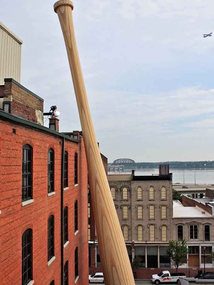 The view from behind reveals the bat's impressive engineering, towering over historic brick buildings like a friendly giant at a garden party.