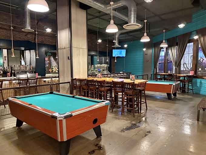 Industrial chic meets vintage charm where pool tables share space with dining tables under pendant lights.