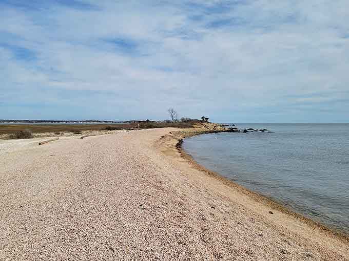 This peaceful shoreline stretches endlessly, where gentle waves meet smooth stones under Connecticut's summer sky.