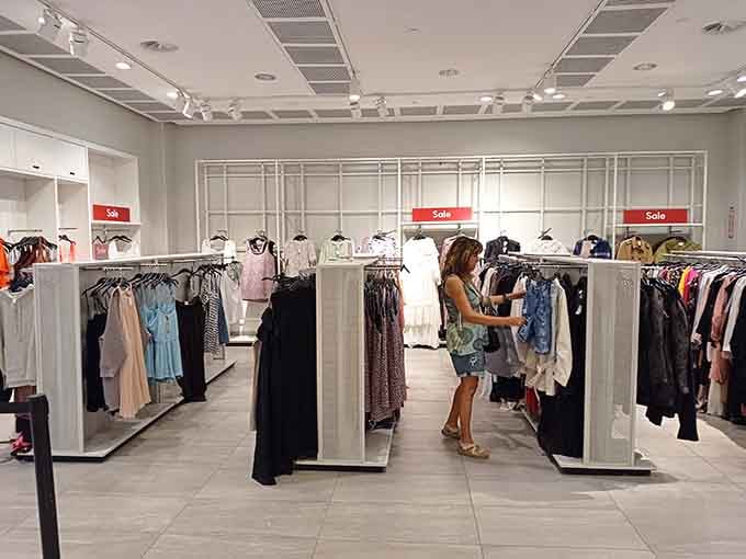 Clean, bright aisles invite you to hunt through racks where designer dreams become affordable realities with every sale sign.