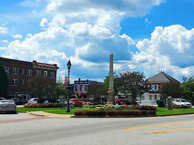 The town square monument stands proudly surrounded by flowers, historic buildings, and that perfect Southern sky above everything.