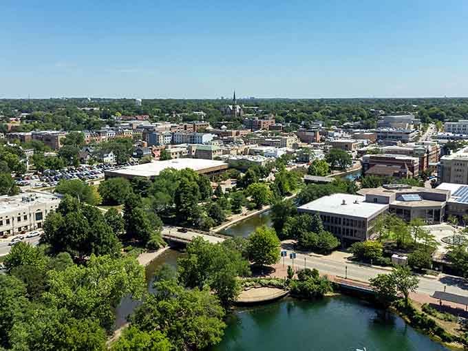 Lush greenery frames this river town vista where church spires pierce blue skies above peaceful neighborhoods.