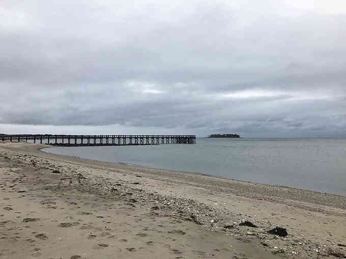 Gray skies and quiet shores create a peaceful scene where the long pier stretches endlessly into calm waters.
