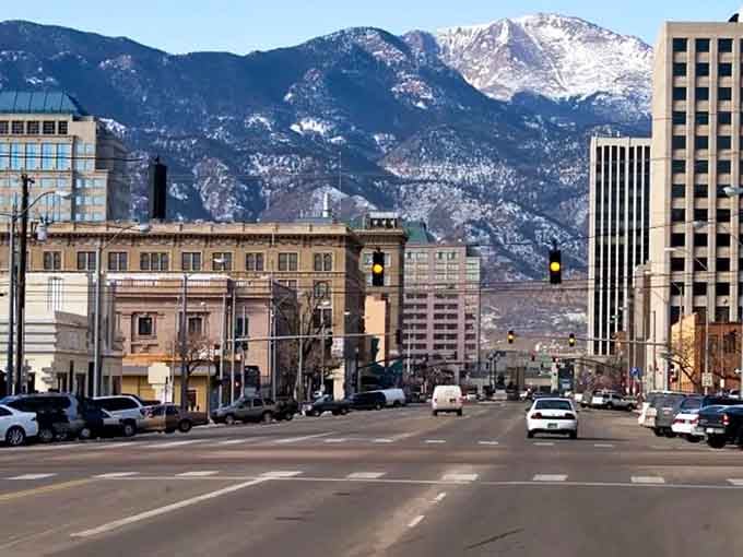 Snow-dusted mountains frame city blocks where urban life meets wilderness in perfect Colorado harmony every single day.