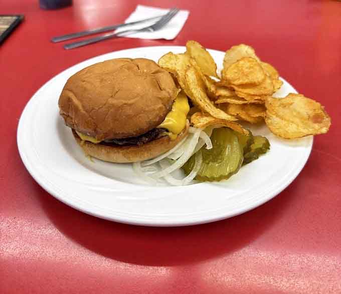 A cheeseburger with kettle chips and pickles proves that sometimes perfection comes on a simple white plate.