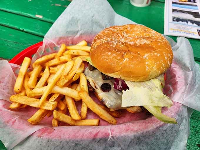 A juicy burger with all the fixings next to golden fries on a bright green table&mdash;California road trip perfection achieved.