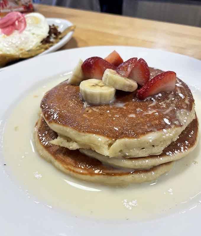 Golden pancakes crowned with fresh strawberries and bananas, proof that perfection exists on a plate.