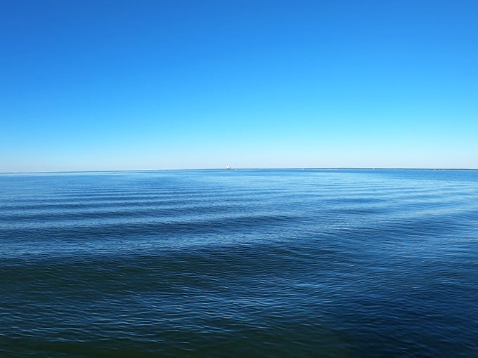 The bay stretches endlessly, calm and inviting, with the lighthouse barely visible on the horizon.