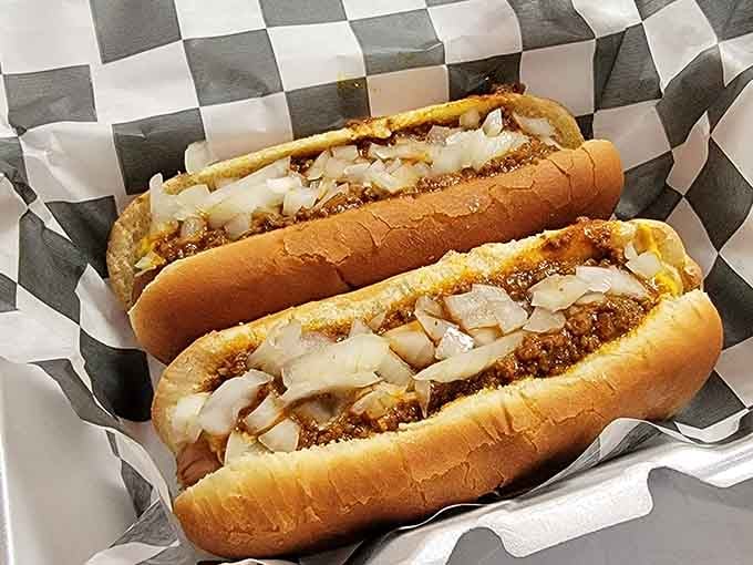 Two hot dogs loaded with chili and onions, nestled in checkered paper like edible treasures waiting to happen.