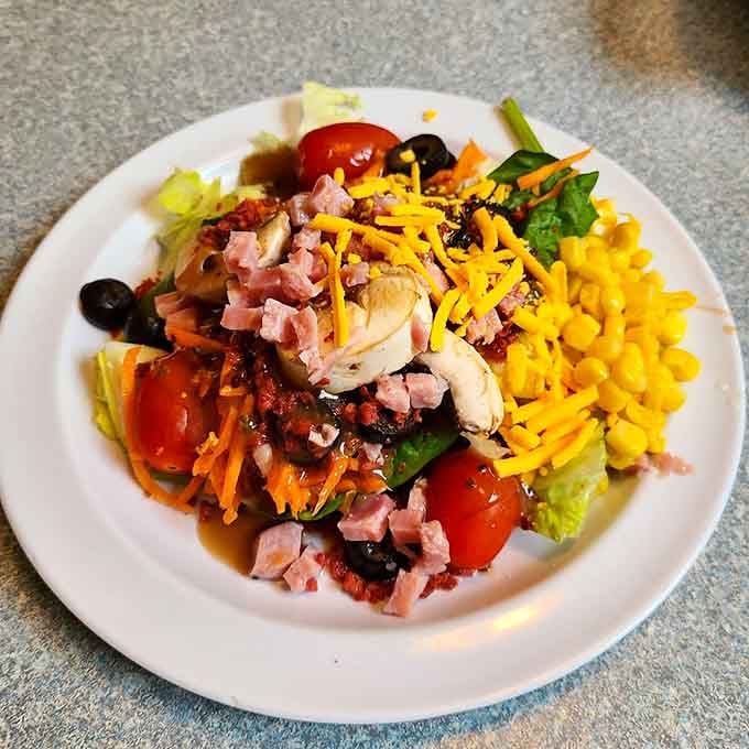 Look at that salad bar creation: bacon, cheese, olives, and tomatoes piled high like edible architecture on a plate.
