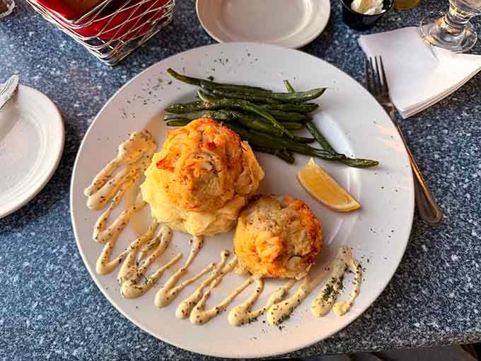 Two golden crab cakes with artistic sauce drizzles and crisp green beans prove that simple perfection never goes out of style.