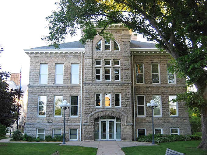 This grand stone courthouse stands like a fortress of democracy, its arched entrance welcoming citizens under shade trees for generations.