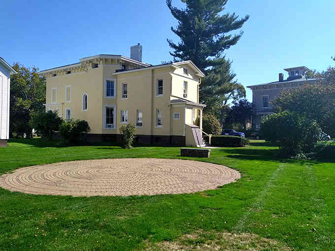 This elegant yellow mansion sits gracefully on manicured lawns, its circular brick pattern adding unexpected artistic flair to the grounds.