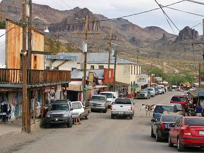 Dramatic mountain peaks tower over weathered storefronts where modern pickups park alongside century-old buildings.