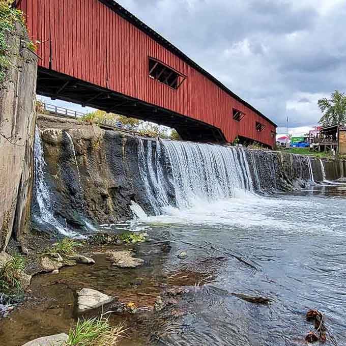 Water cascades beneath weathered red wood, creating a postcard moment that covered bridges were practically invented to frame.
