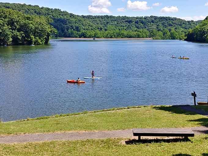 Paddleboarders and kayakers glide across glassy water surrounded by green hills that seem to hug the lake.