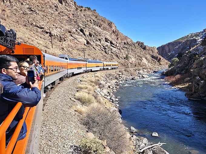 Passengers lean out from the open-air observation car, cameras ready, as the river rushes alongside this scenic canyon route.