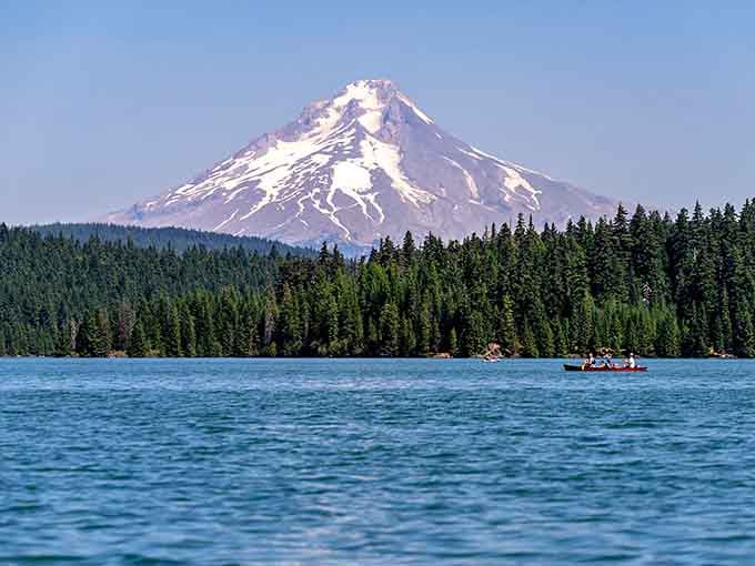 A lone boat drifts across crystal-clear water with Mount Hood standing guard in the distance.