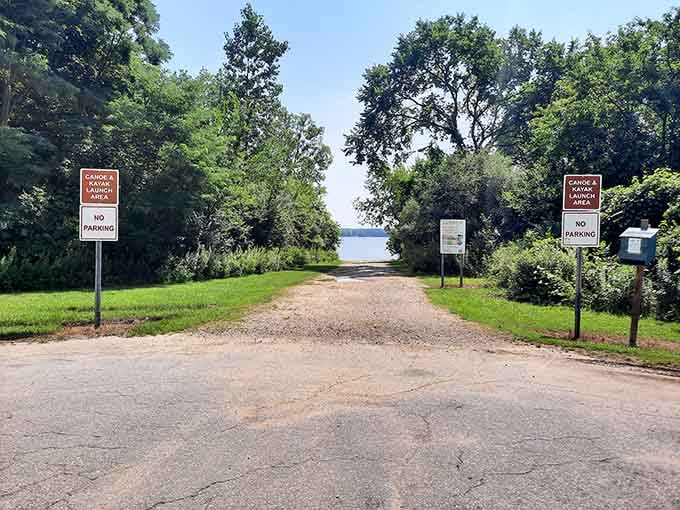 The boat launch beckons adventurers through a tree-lined corridor that promises aquatic escapades just beyond those signs.