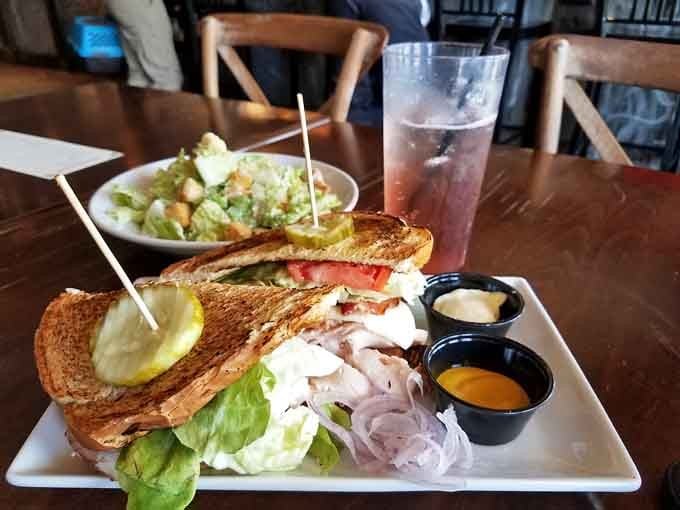 This towering sandwich arrives with multiple dipping sauces because choices matter, even during lunch breaks.