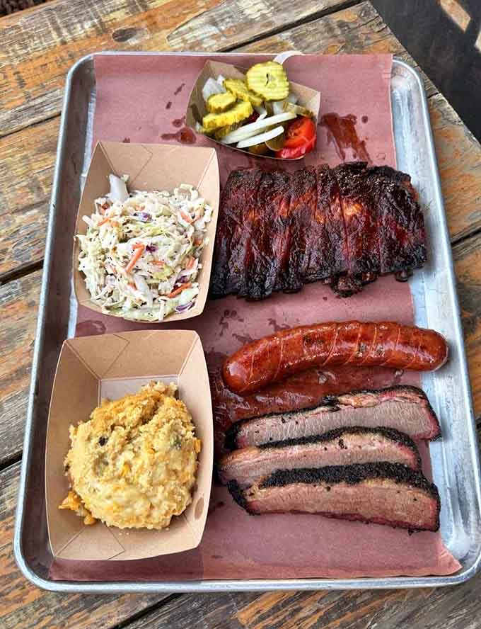 A metal tray loaded with brisket, ribs, sausage, and sides is basically a love letter written in smoke and spice.