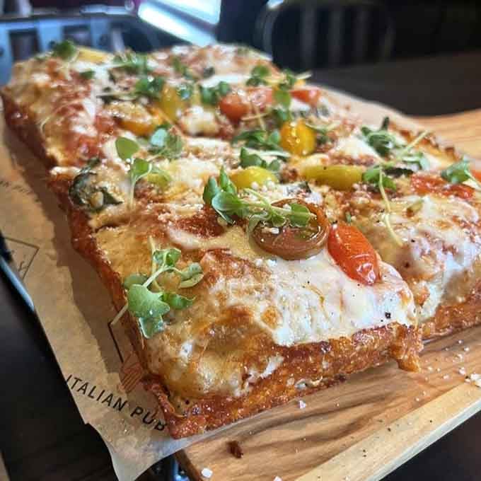 Behold the Roman-style pizza in all its rectangular glory, topped with colorful heirloom tomatoes and fresh herbs.