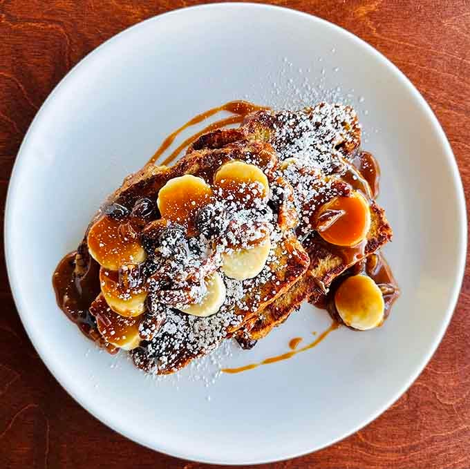 French toast topped with bananas, powdered sugar, and caramel drizzle that'll make you forget every other breakfast you've ever had.