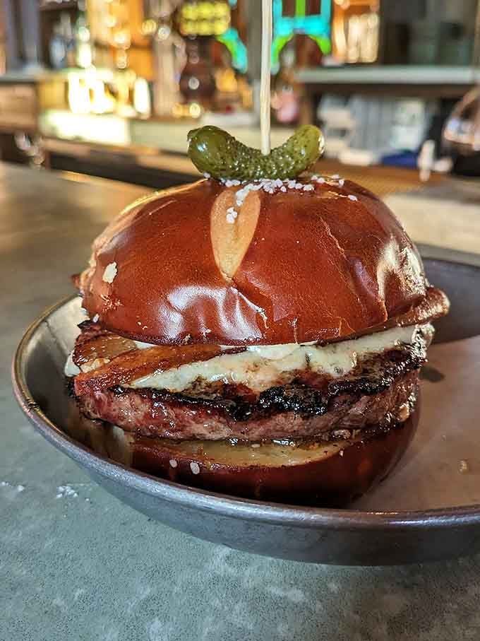 Look at that glistening pretzel bun cradling pure beef bliss, topped with pickles that add the perfect tangy crunch.