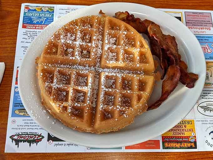 That waffle's golden grid pattern holds pockets of pure joy, dusted with powdered sugar like edible snowfall.
