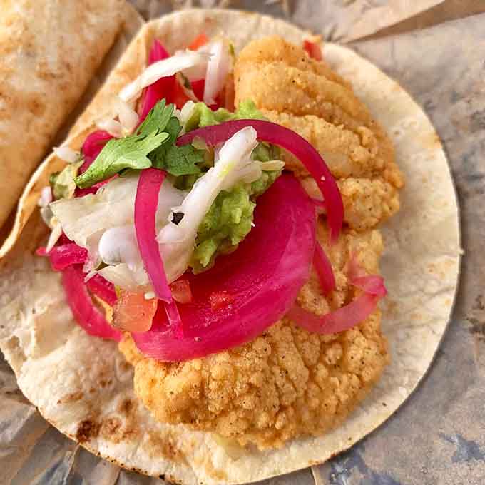 Fish tacos get the gourmet treatment with pickled onions so vibrant they practically glow with flavor potential.