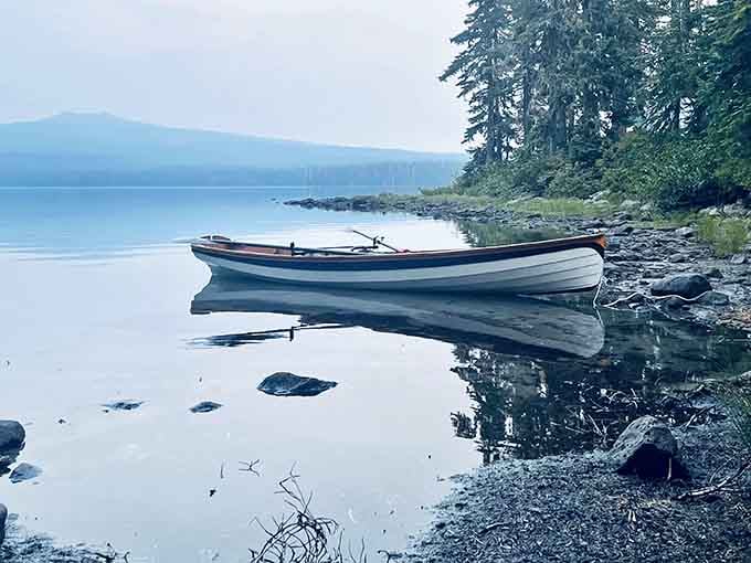A lone boat rests in mirror-perfect stillness, waiting for someone brave enough to face that ice-cold water.