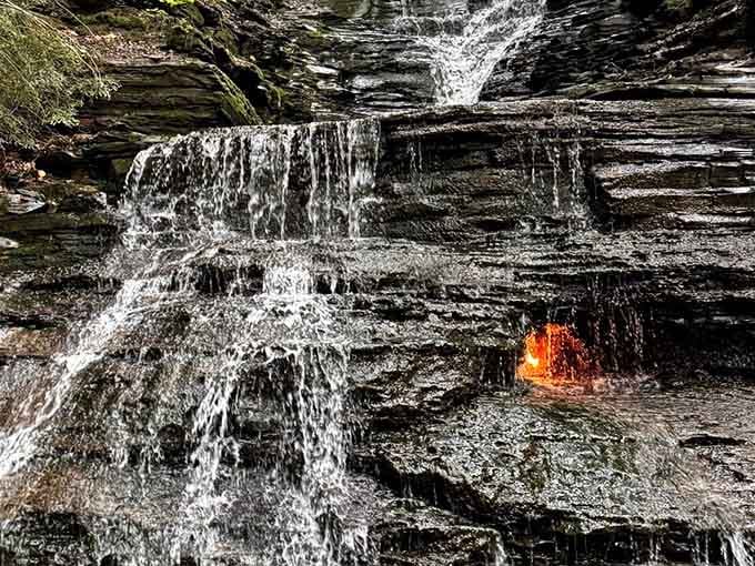 Fire and water meet in nature's impossible magic trick, flickering orange flames dancing behind cascading curtains of water.